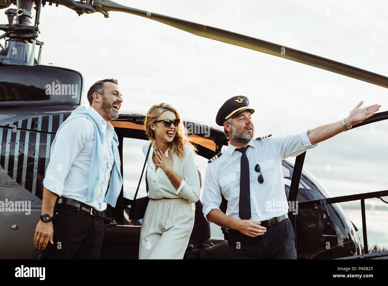 Beautiful couple standing by helicopter with pilot pointing at ...