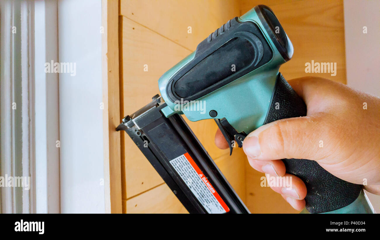 Carpenter brad using nail gun to moldings on windows, framing trim ...