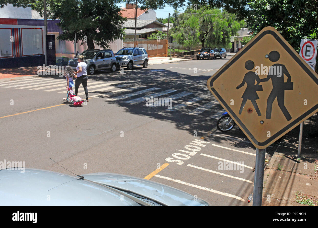 Pais e estudantes atravessam rua próximo a placa indicativa de ...