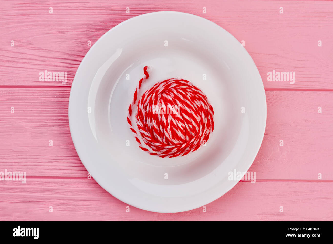 Ball of yarn on white plate. Ball of red woolen thread on porcelain ...