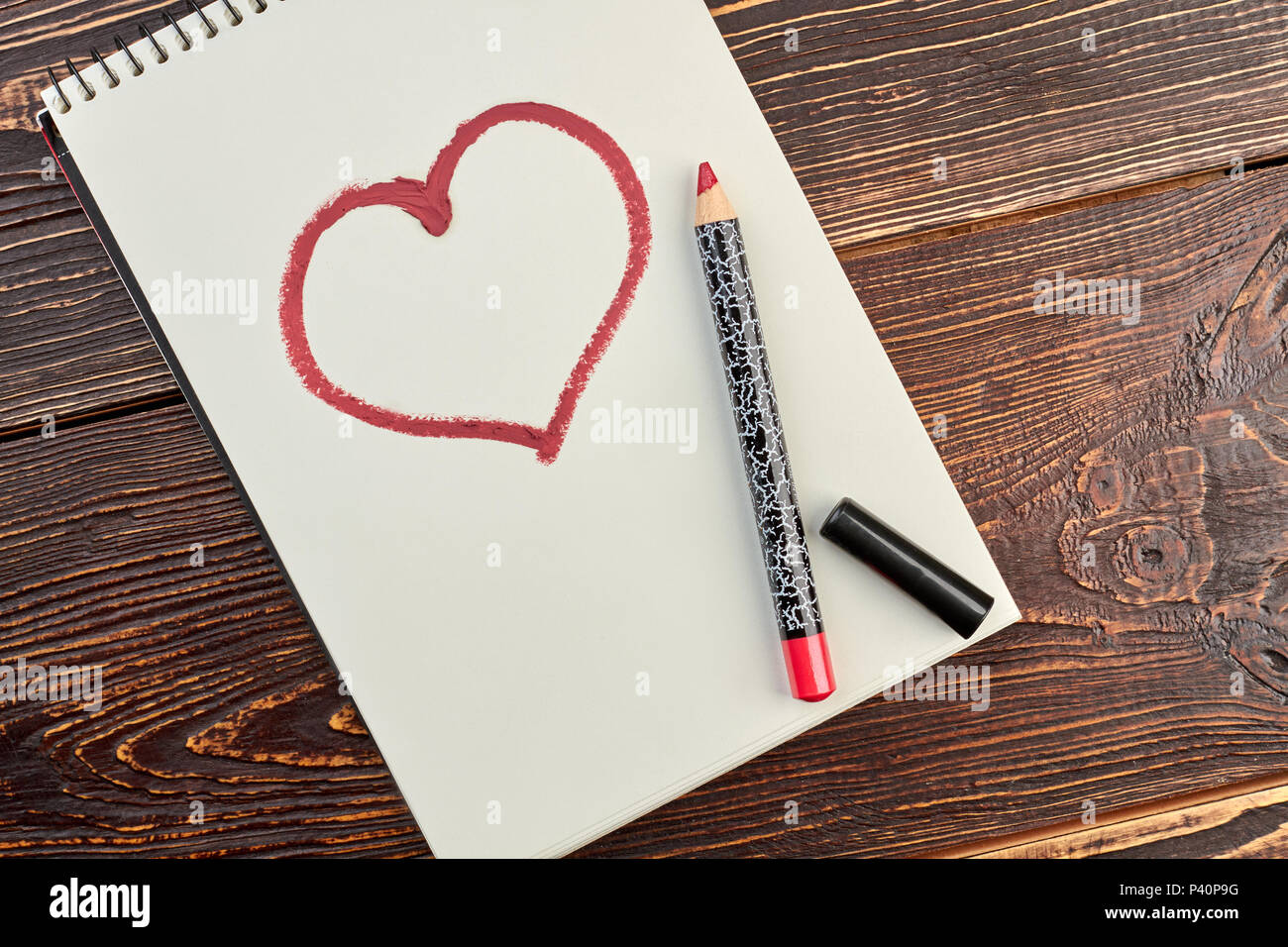 White paper notebook with drawn heart. Red makeup pencil on white paper ...