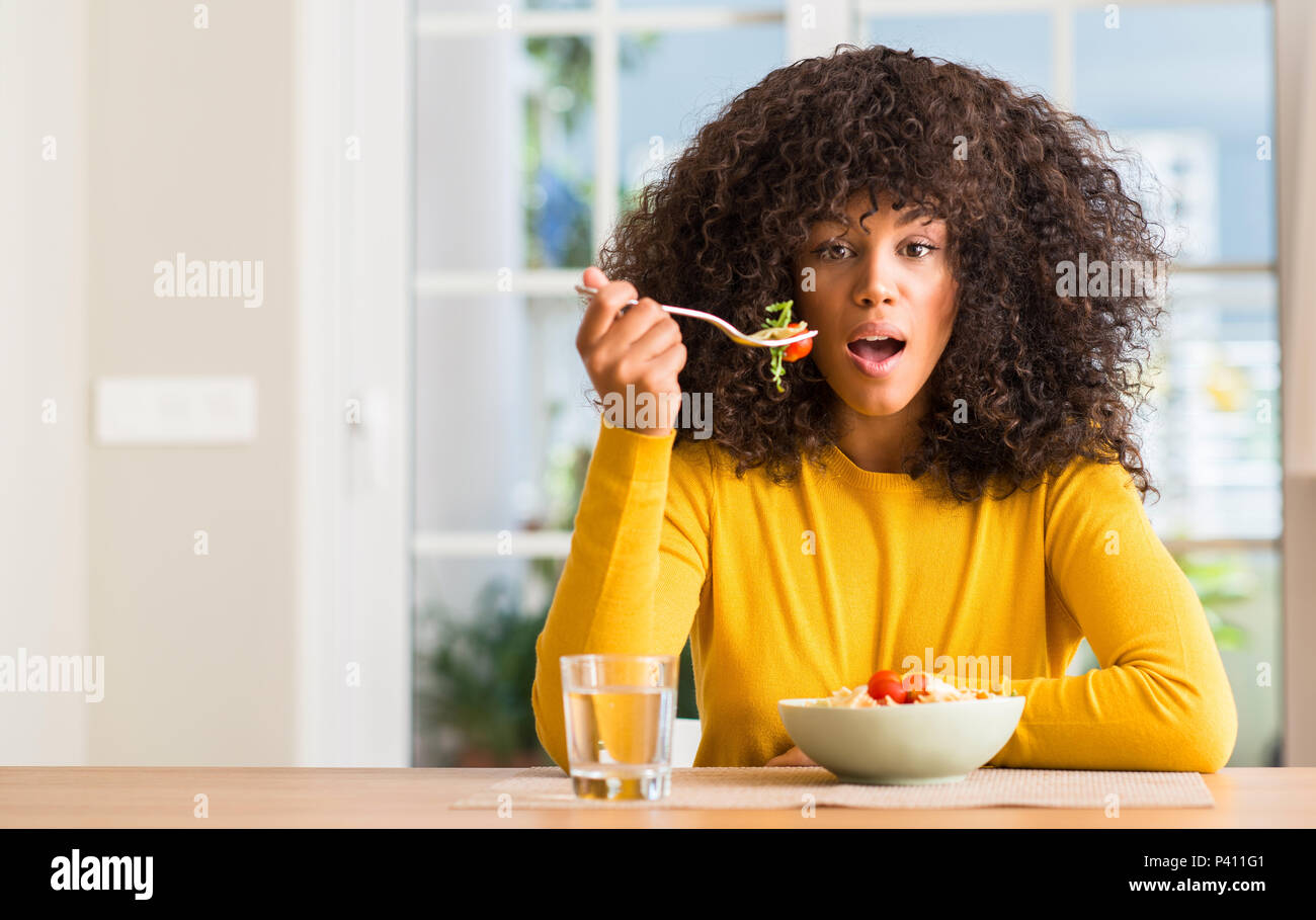 African american woman eating pasta salad at home scared in shock with ...