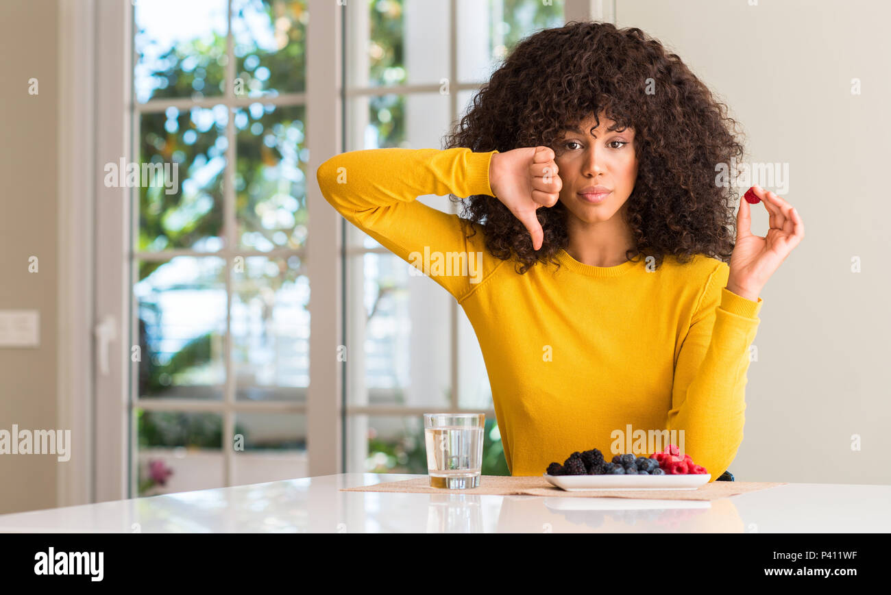 African american woman eating raspberries and blueberries at home with ...