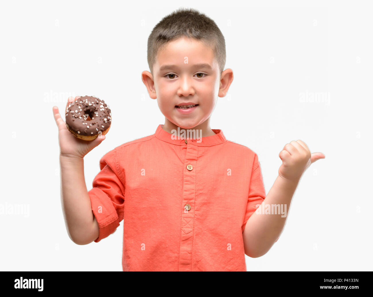 Dark haired little child eating doughnut pointing with hand and finger ...