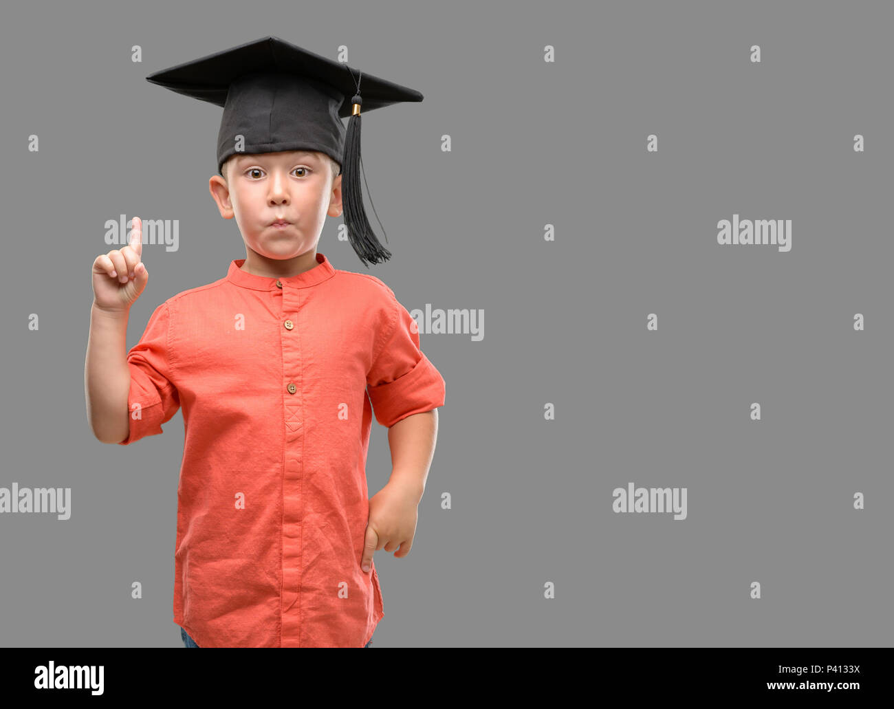 Dark haired little child wearing graduation cap surprised with an idea ...
