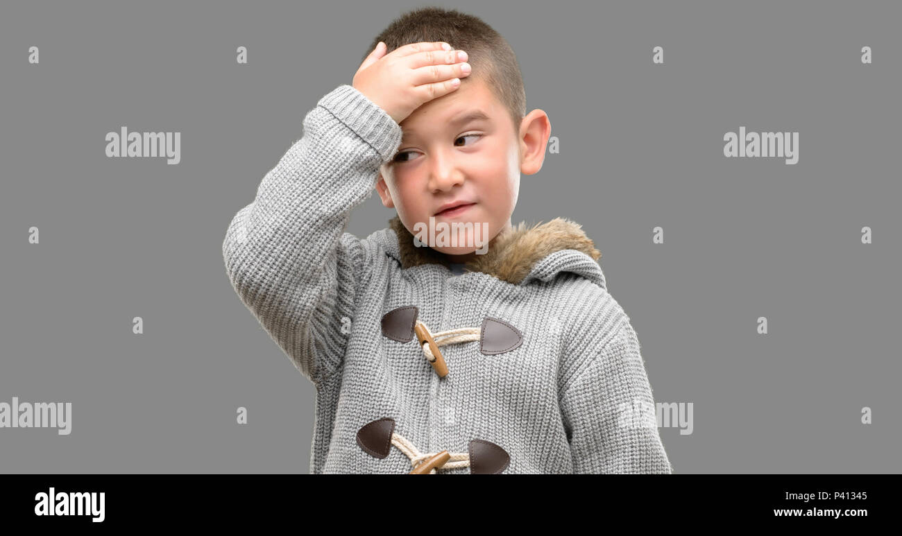 Dark haired little child wearing a coat stressed with hand on head ...