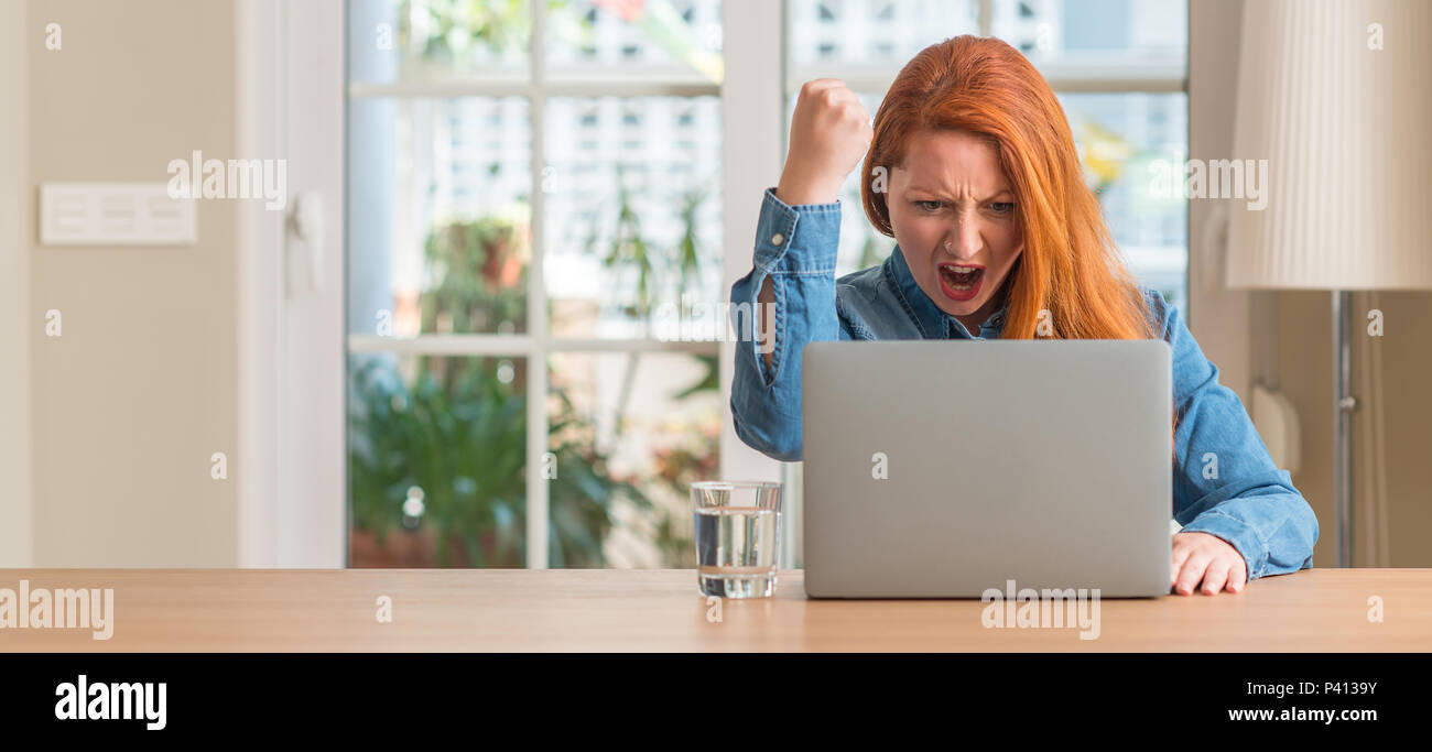Redhead woman using computer laptop at home annoyed and frustrated ...