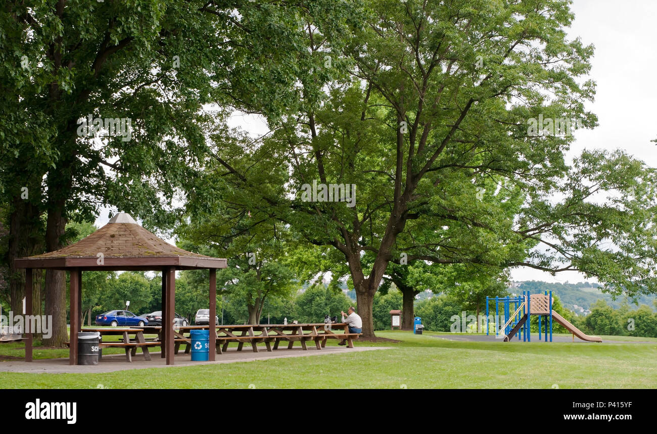 A man sitting at a park table reading at the Schenley Park playground ...