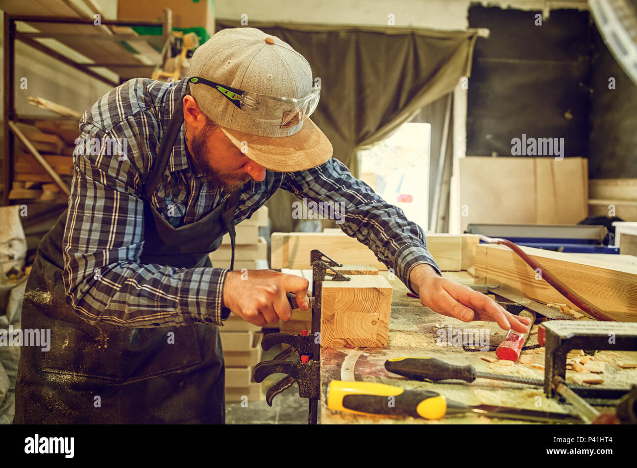 Strong carpenter in work clothes carving wood using a woodworking tool ...