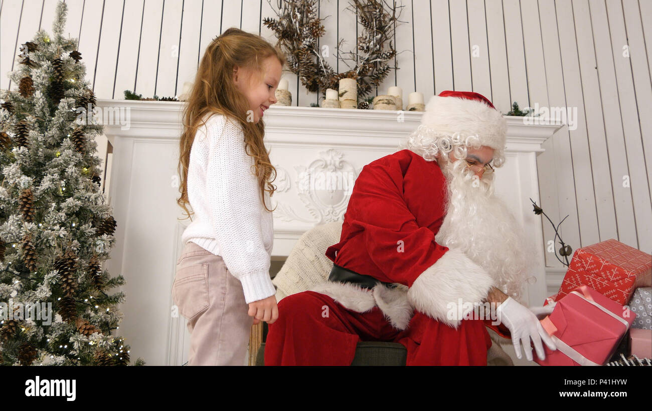 Little girl bringing a present for Santa and hugging him in his ...