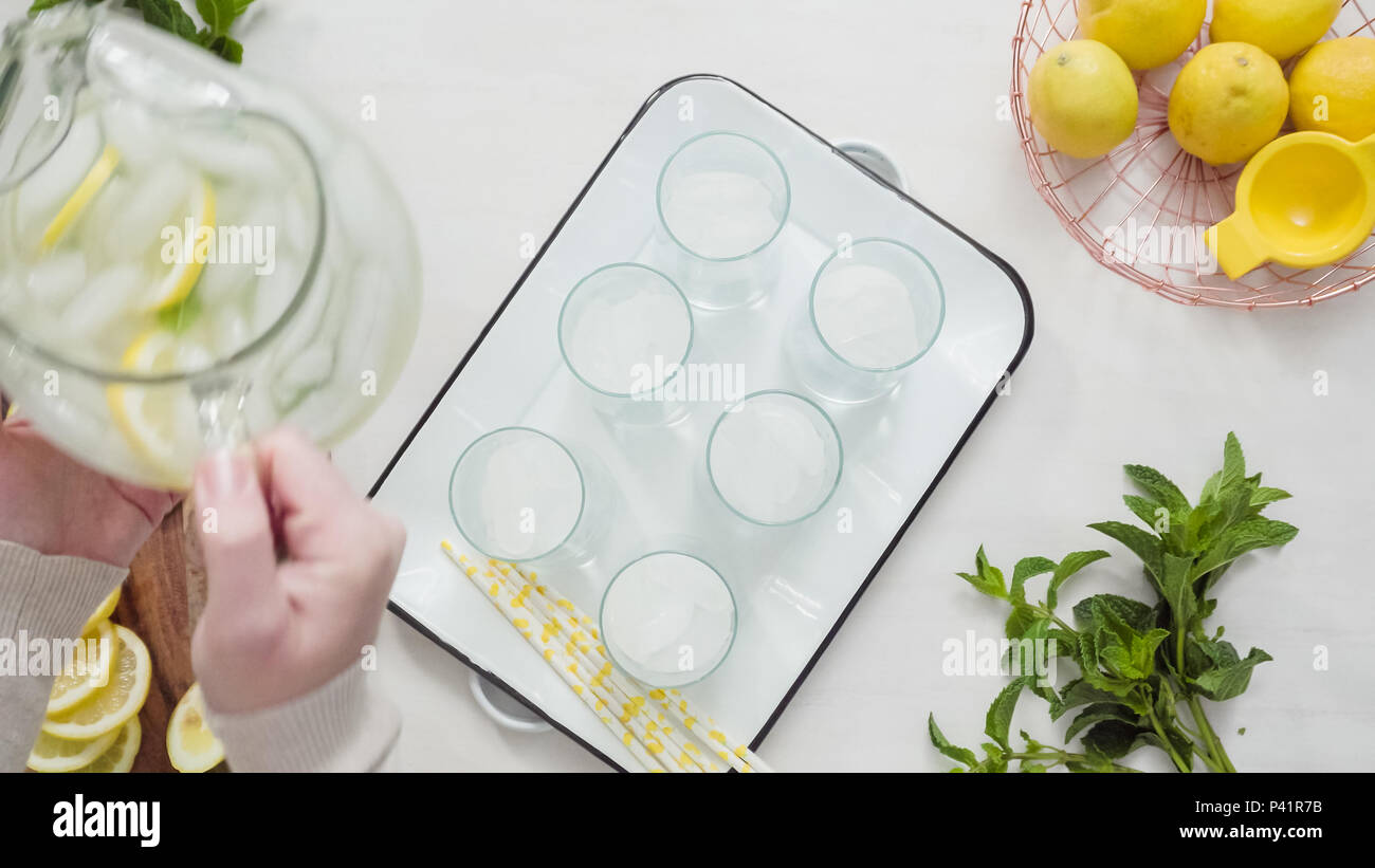 Pouring traditional lemonade with fresh sliced lemons and mint into the ...