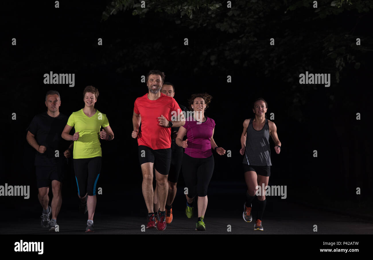 group of healthy people jogging in city park, runners team at night ...