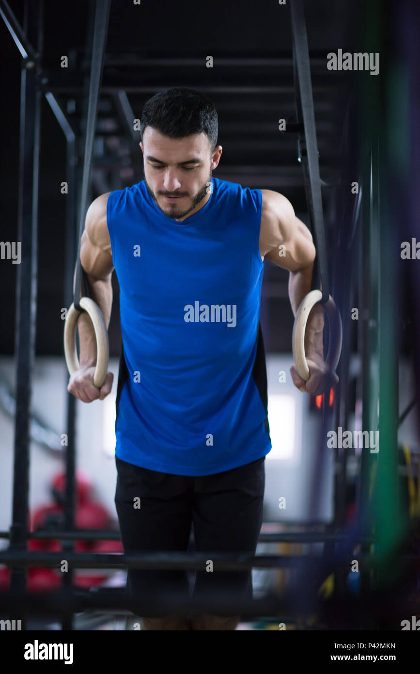 young athlete man working out pull ups with gymnastic rings at the ...