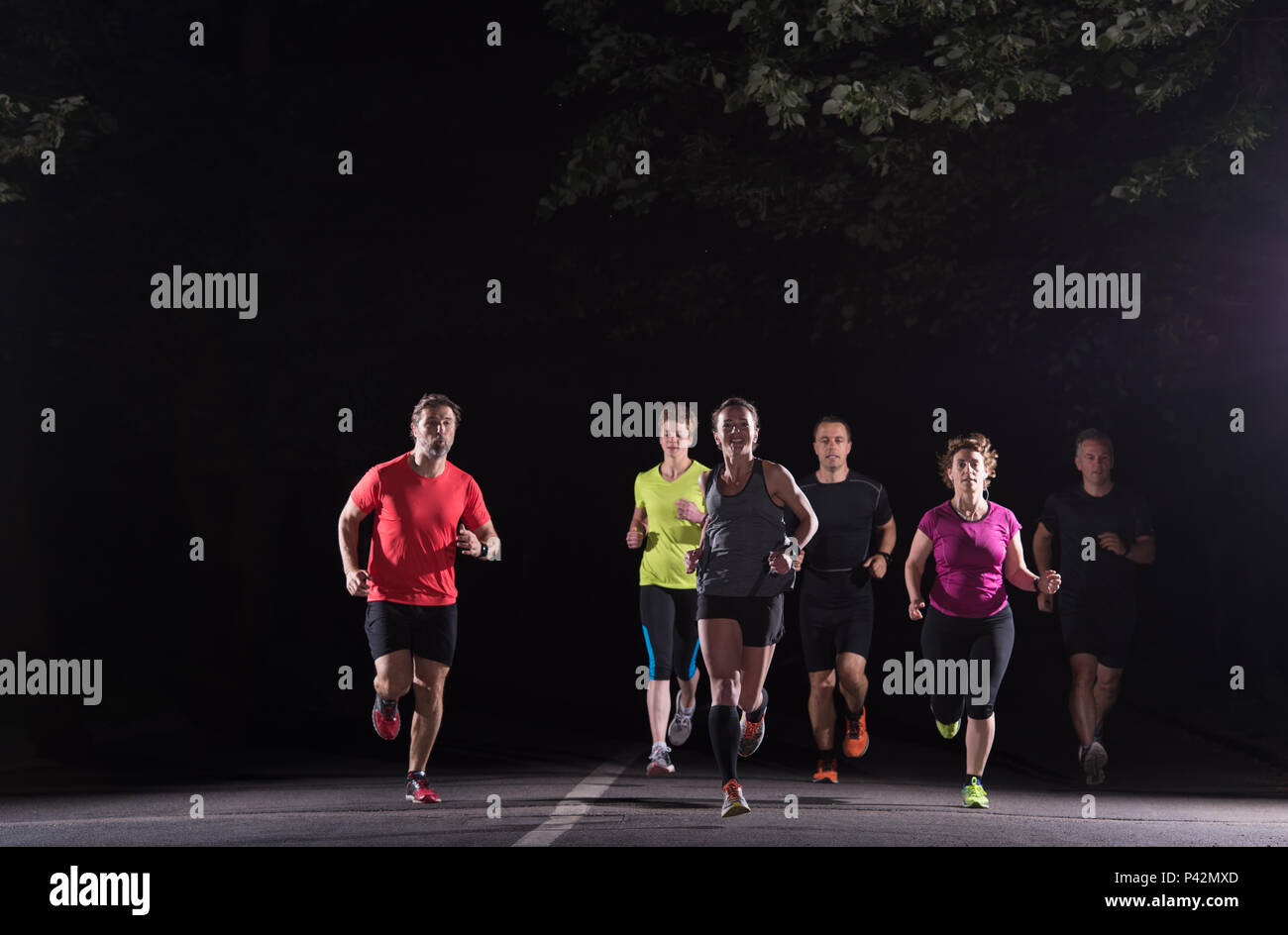 group of healthy people jogging in city park, runners team at night ...