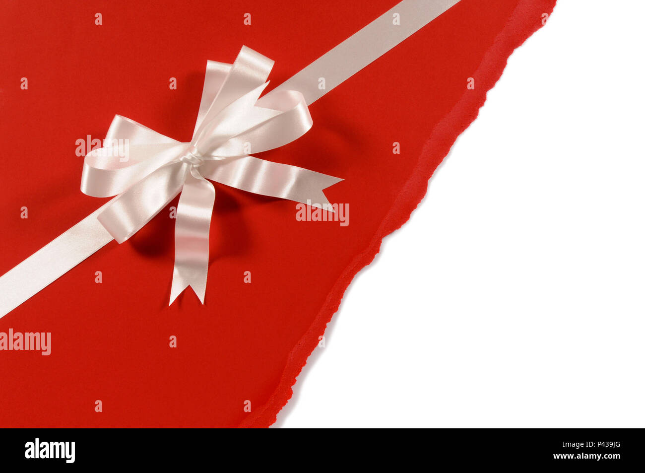 Gift ribbon and bow in white satin on untidy torn red paper background ...