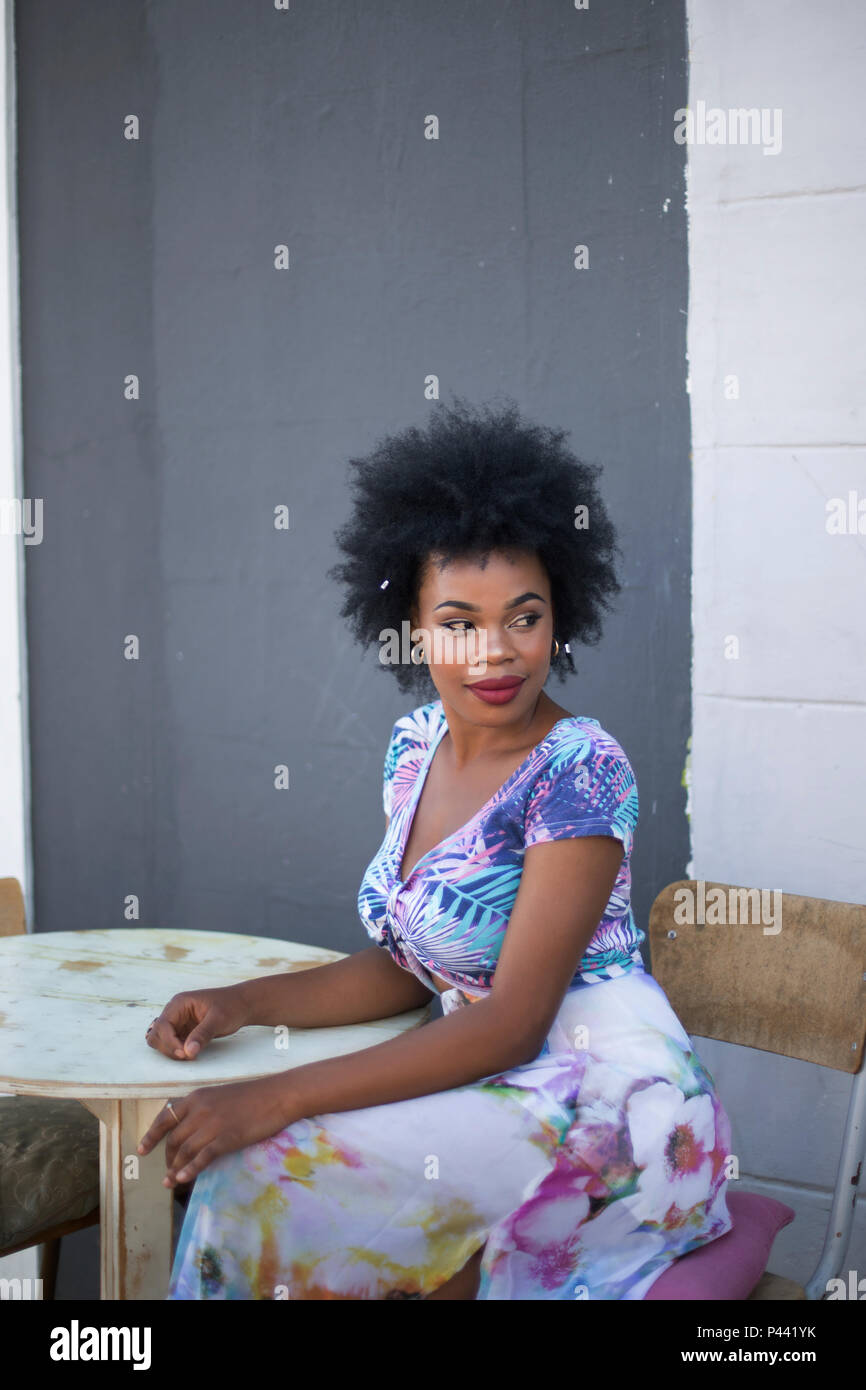 An African model poses while sitting at a table in a floral crop top ...