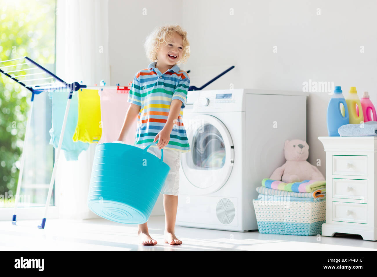 Child in laundry room with washing machine or tumble dryer. Kid helping ...