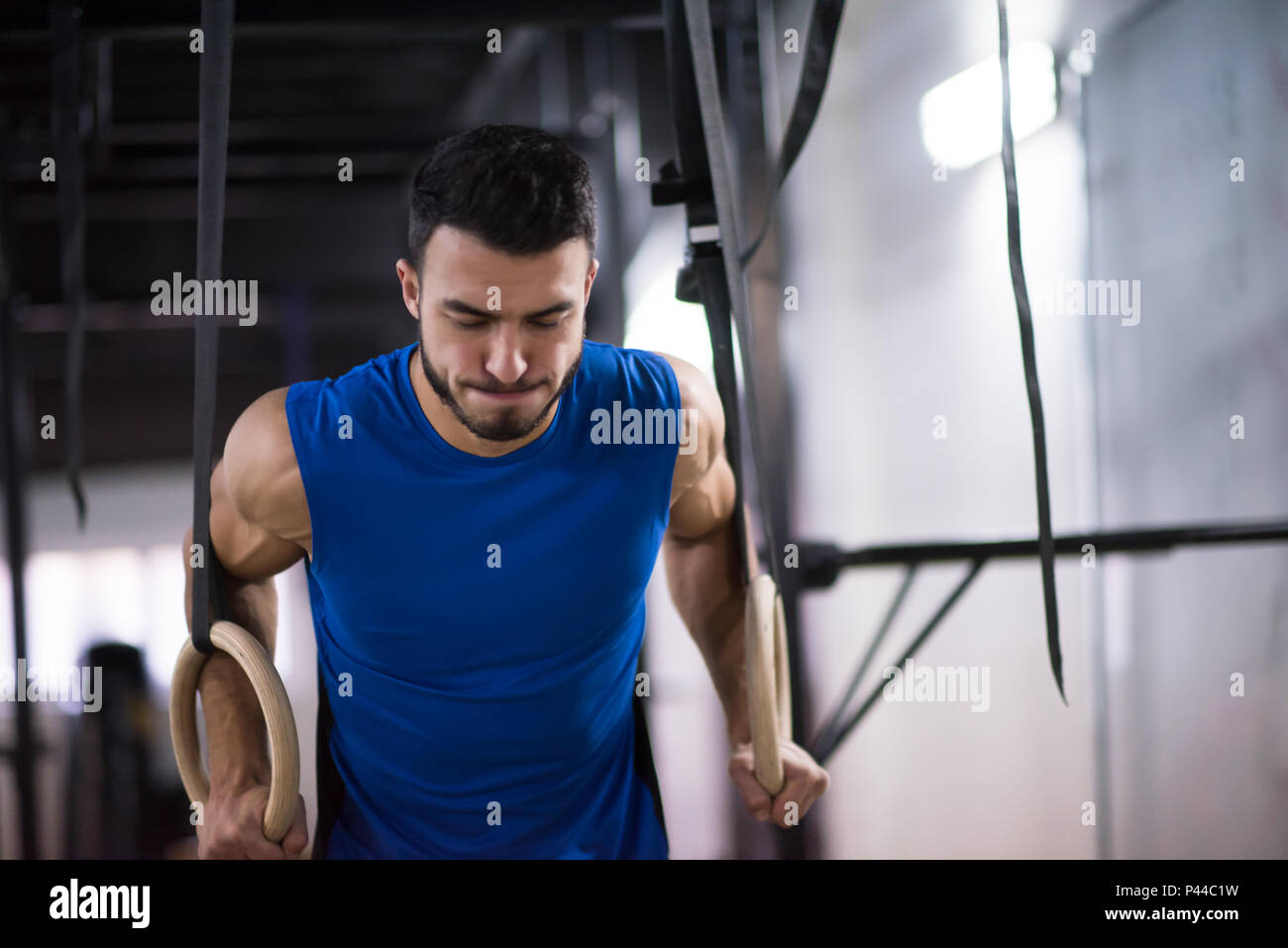 young athlete man working out pull ups with gymnastic rings at the ...