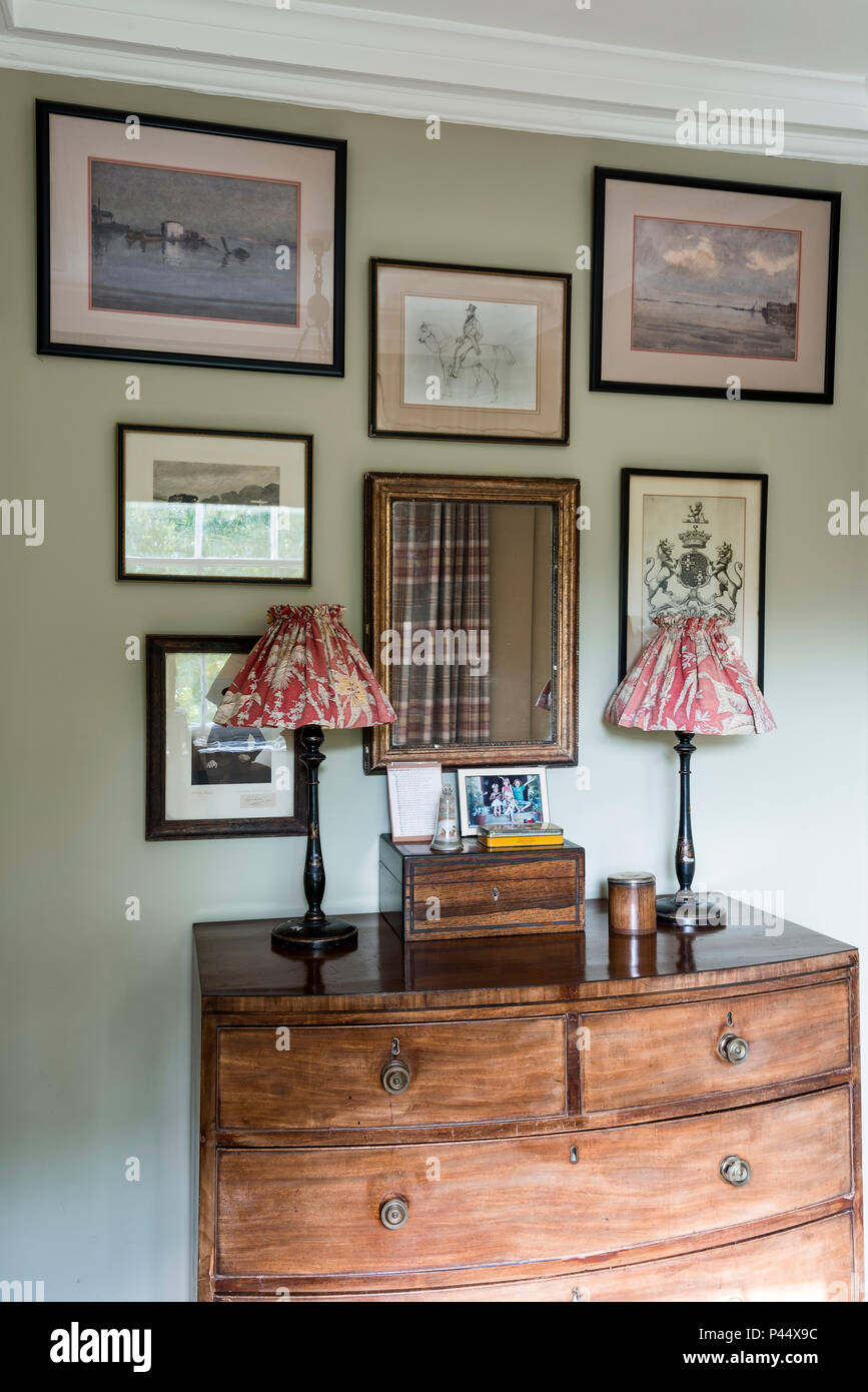 Collection of framed artwork above vintage chest with lamps Stock Photo ...