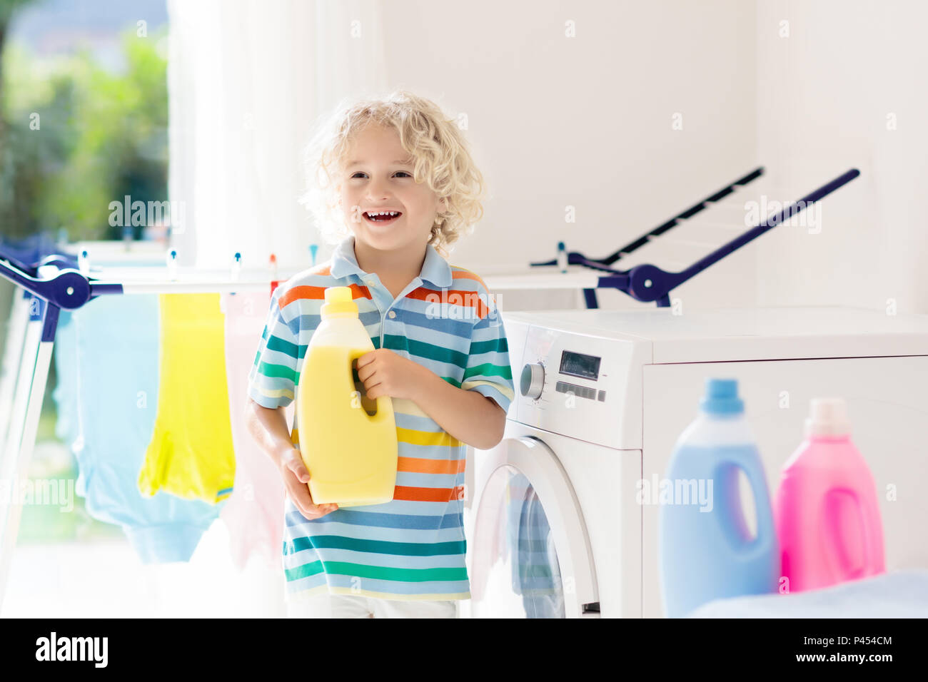 Child in laundry room with washing machine or tumble dryer. Kid helping ...