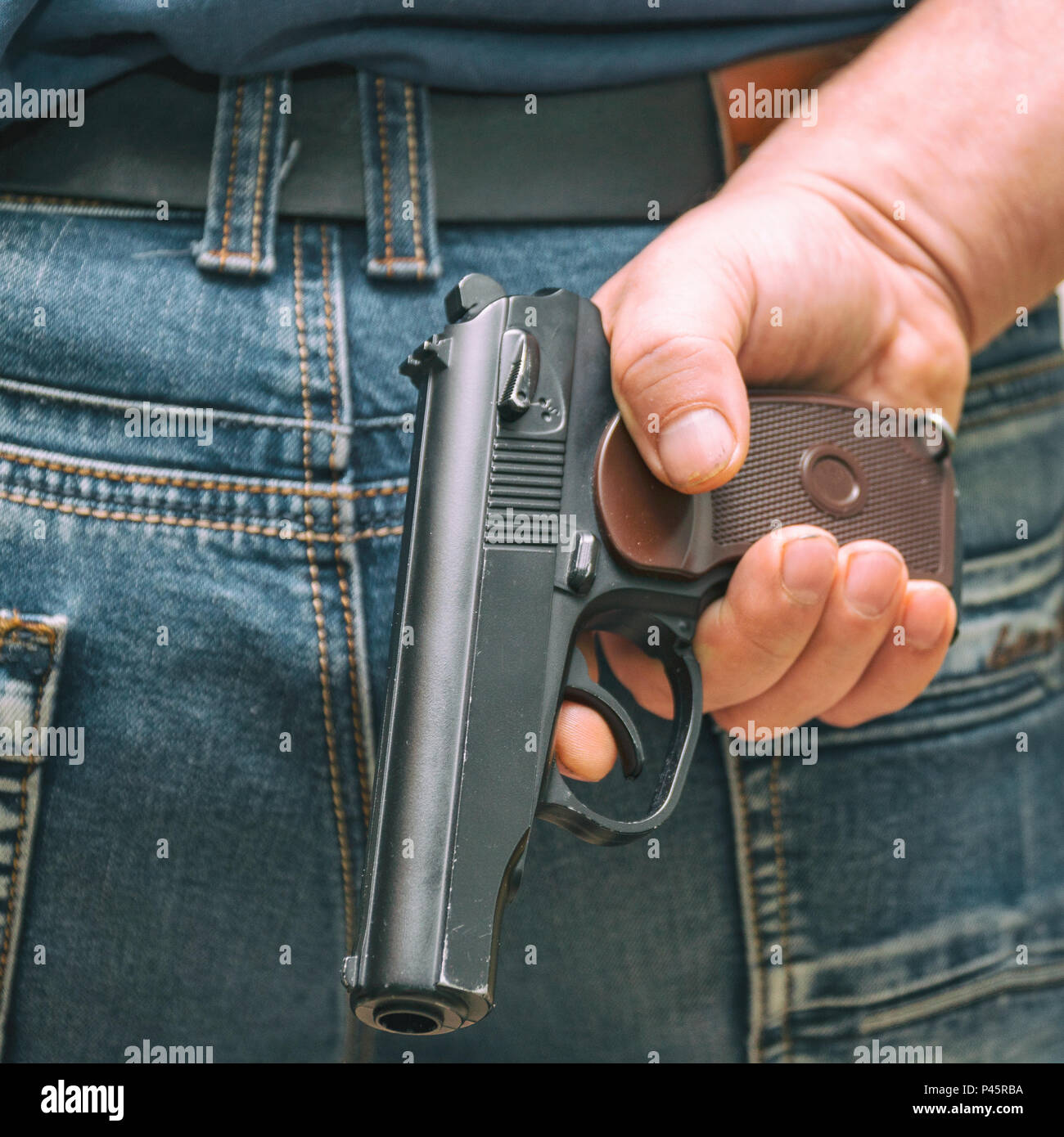 Man in jeans holding a gun behind his back Stock Photo - Alamy