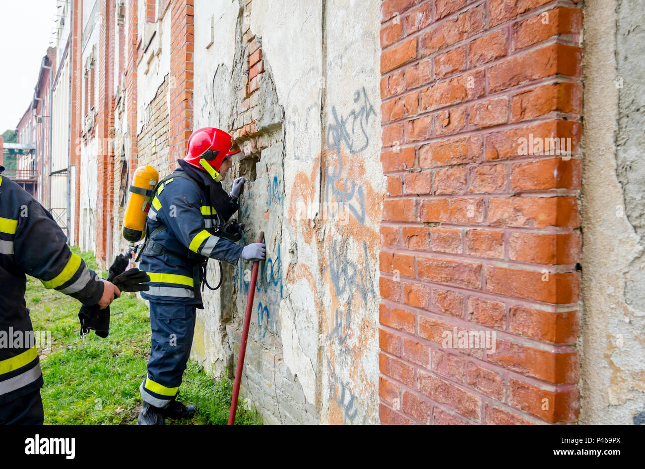 Firefighter is looking through hole that he made in a brick wall ...