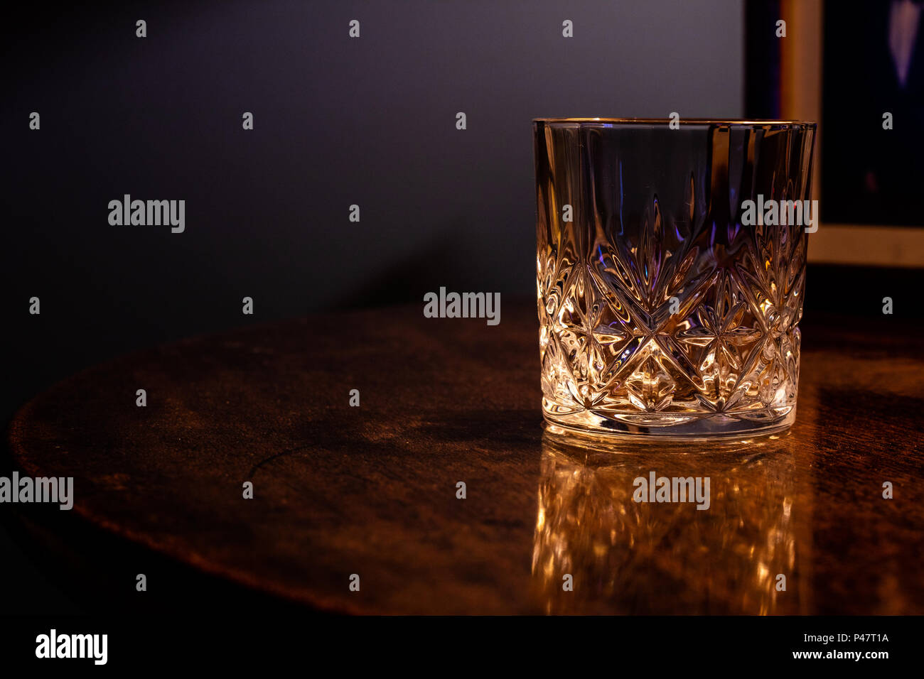 An empty crystal glass resting on on a table with a dark wood grain ...
