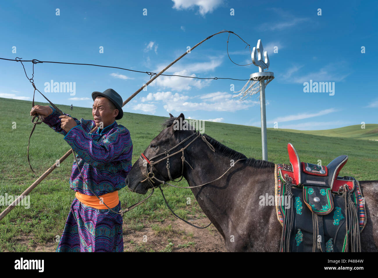 Horseman dressed in traditional costume carries rope and pole urga or ...
