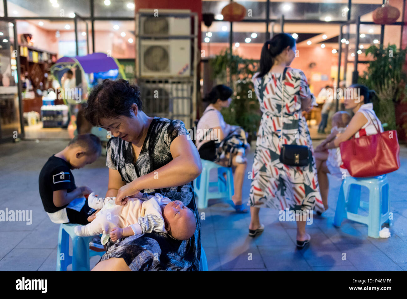 Mother checks diaper as son and friends wait outside restaurant, night ...