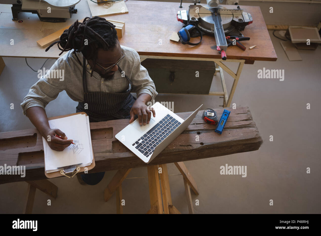 High angle view of carpenter writing in clipboard while using laptop ...