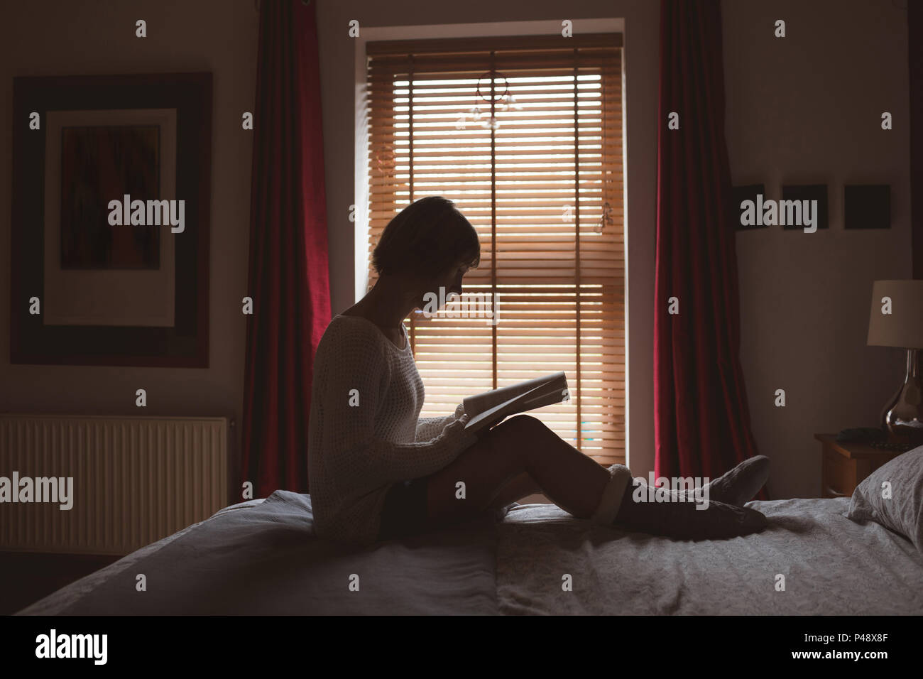Woman reading book on bed in bedroom Stock Photo - Alamy