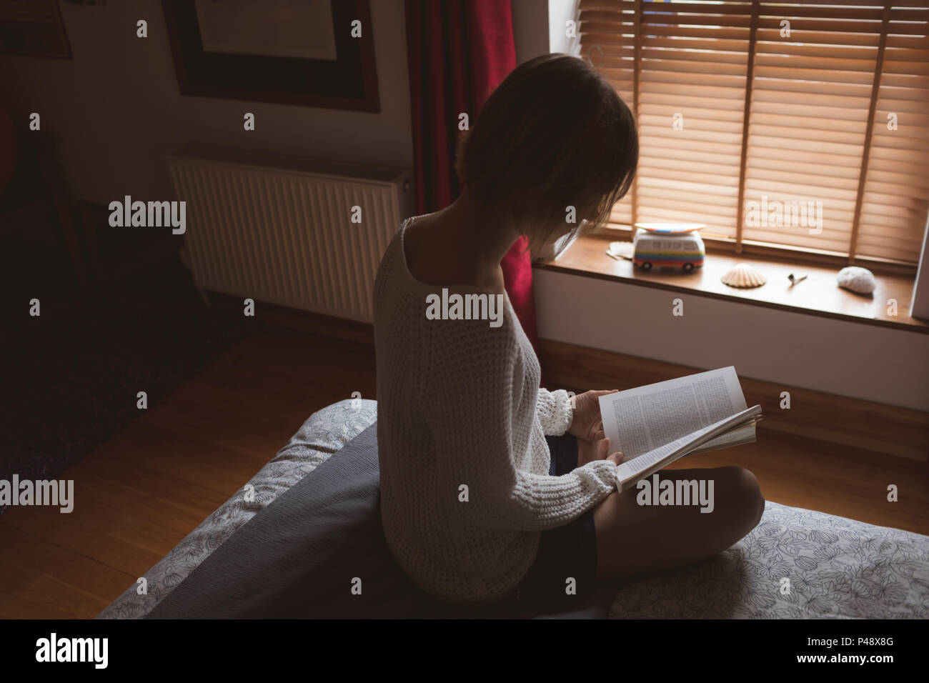 Woman reading book on bed in bedroom Stock Photo - Alamy