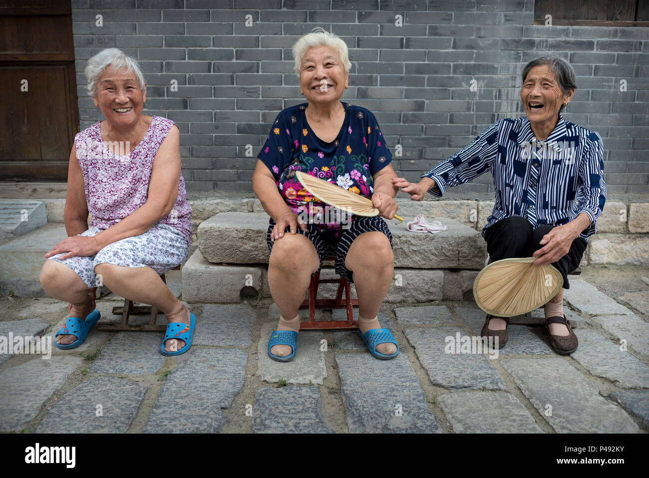 Women friends share a laugh and fan themselves in street at end of hot ...