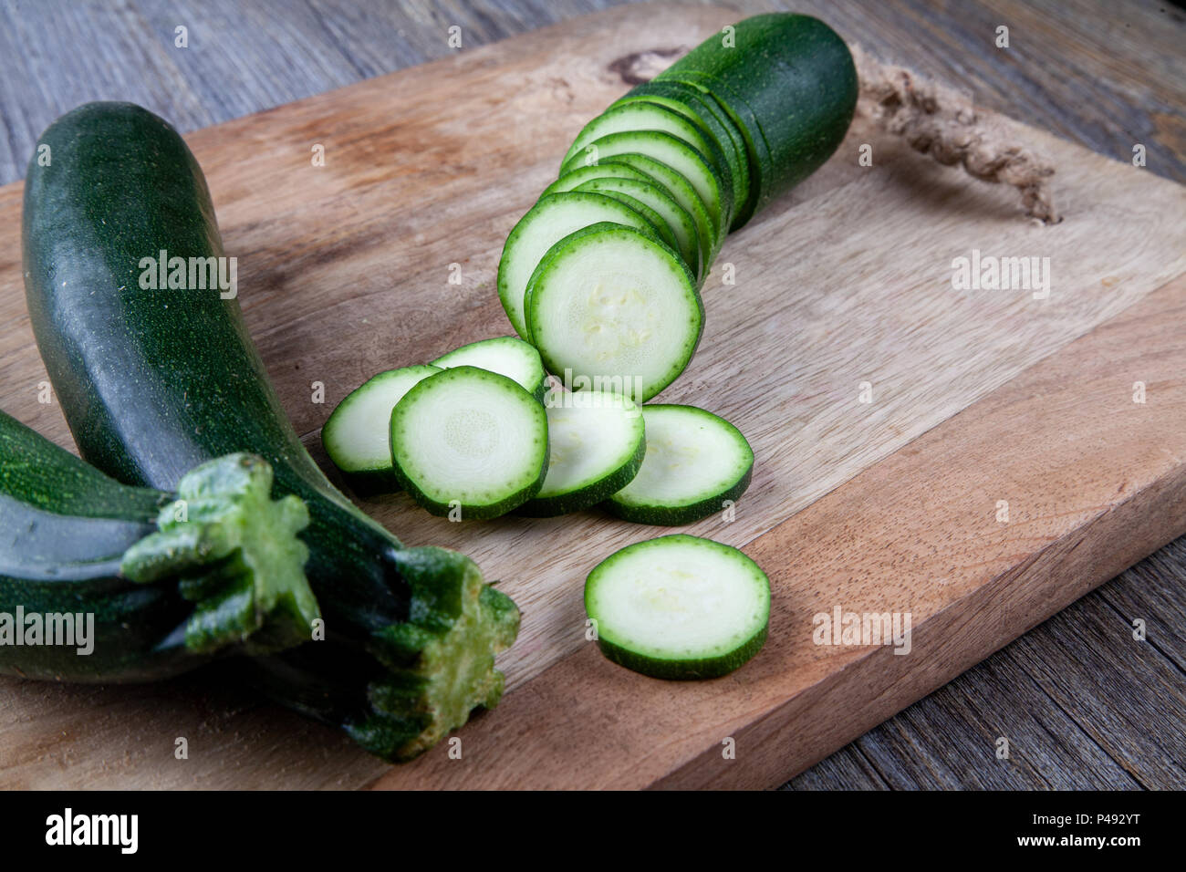Two Courgettes on a wooden chopping board and another sliced courgette ...
