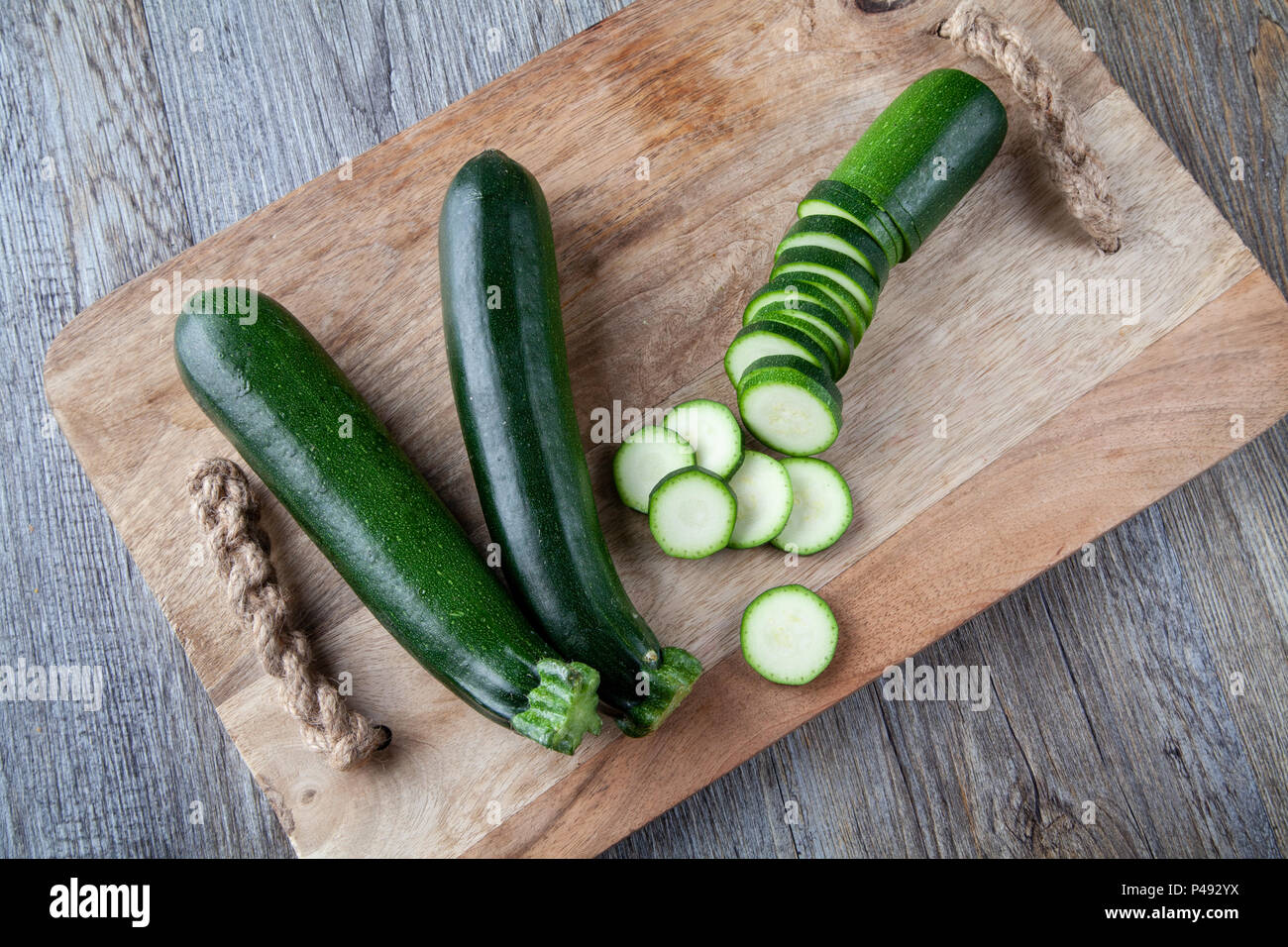 Top view ofTwo Courgettes on a wooden chopping board and another sliced ...