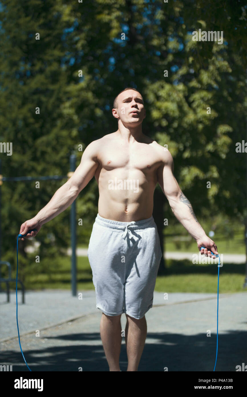 Athletic muscular man jumping with a rope, workout outdoors at sunny ...