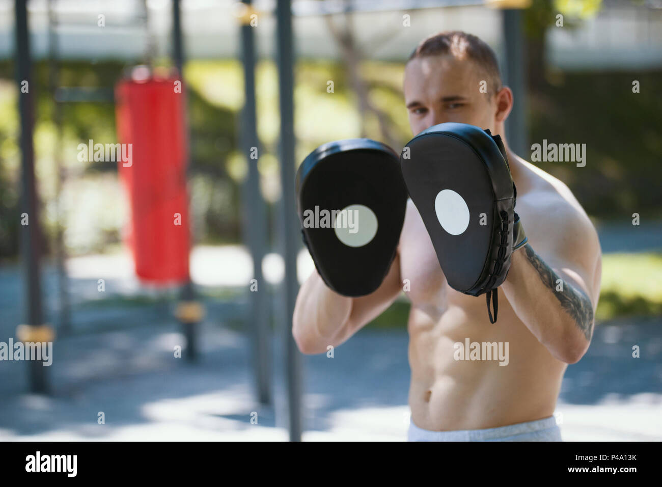 Muscular man boxer in boxing paws, workout in summer park Stock Photo ...