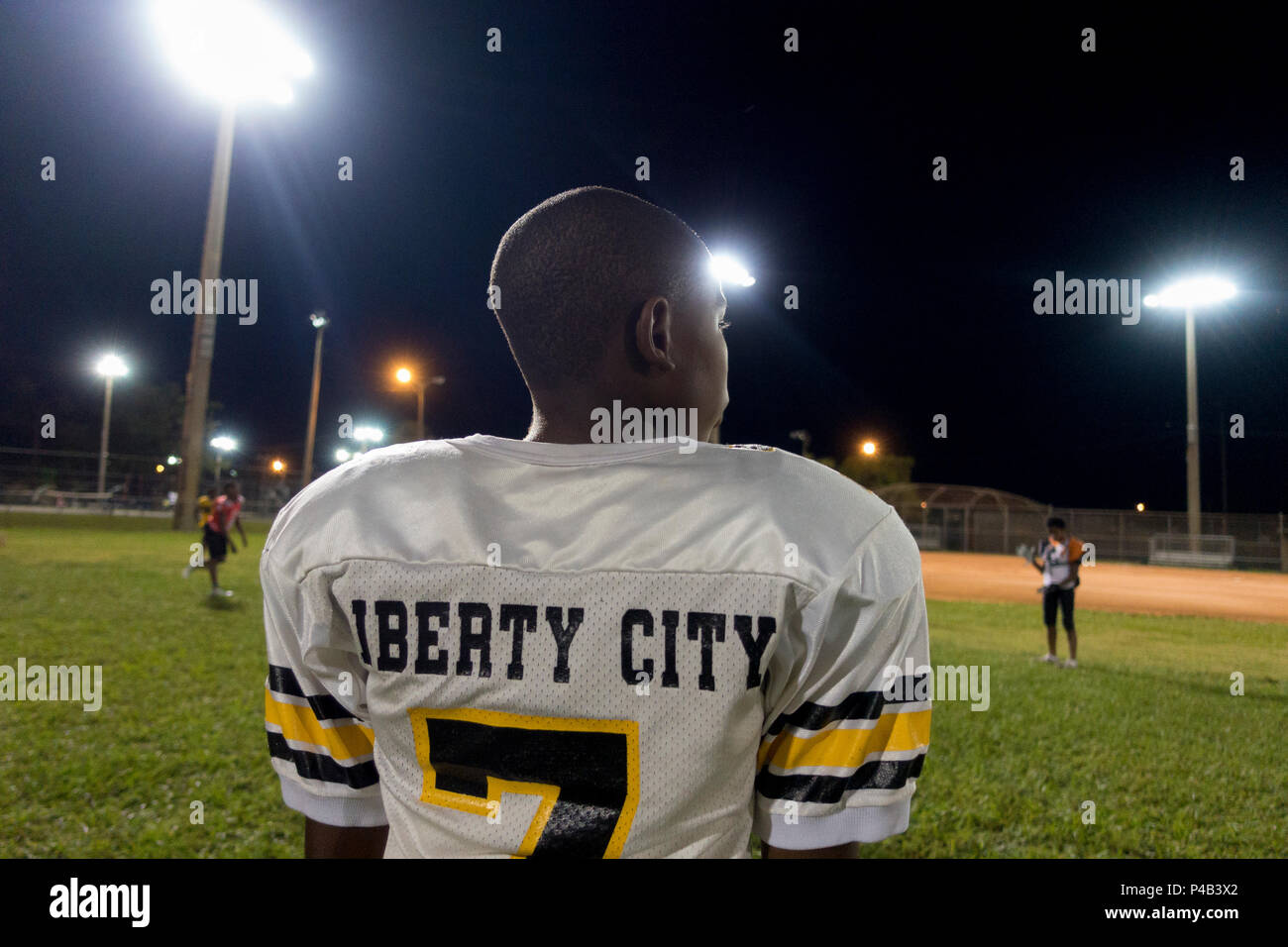 Young boy in football uniform watches team mates play on field at night ...