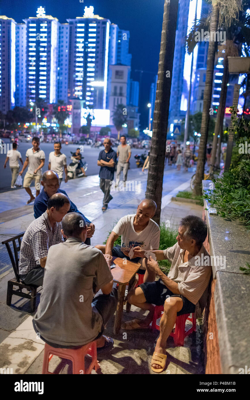 Retired men play game of cards at brightly lit town square on hot ...