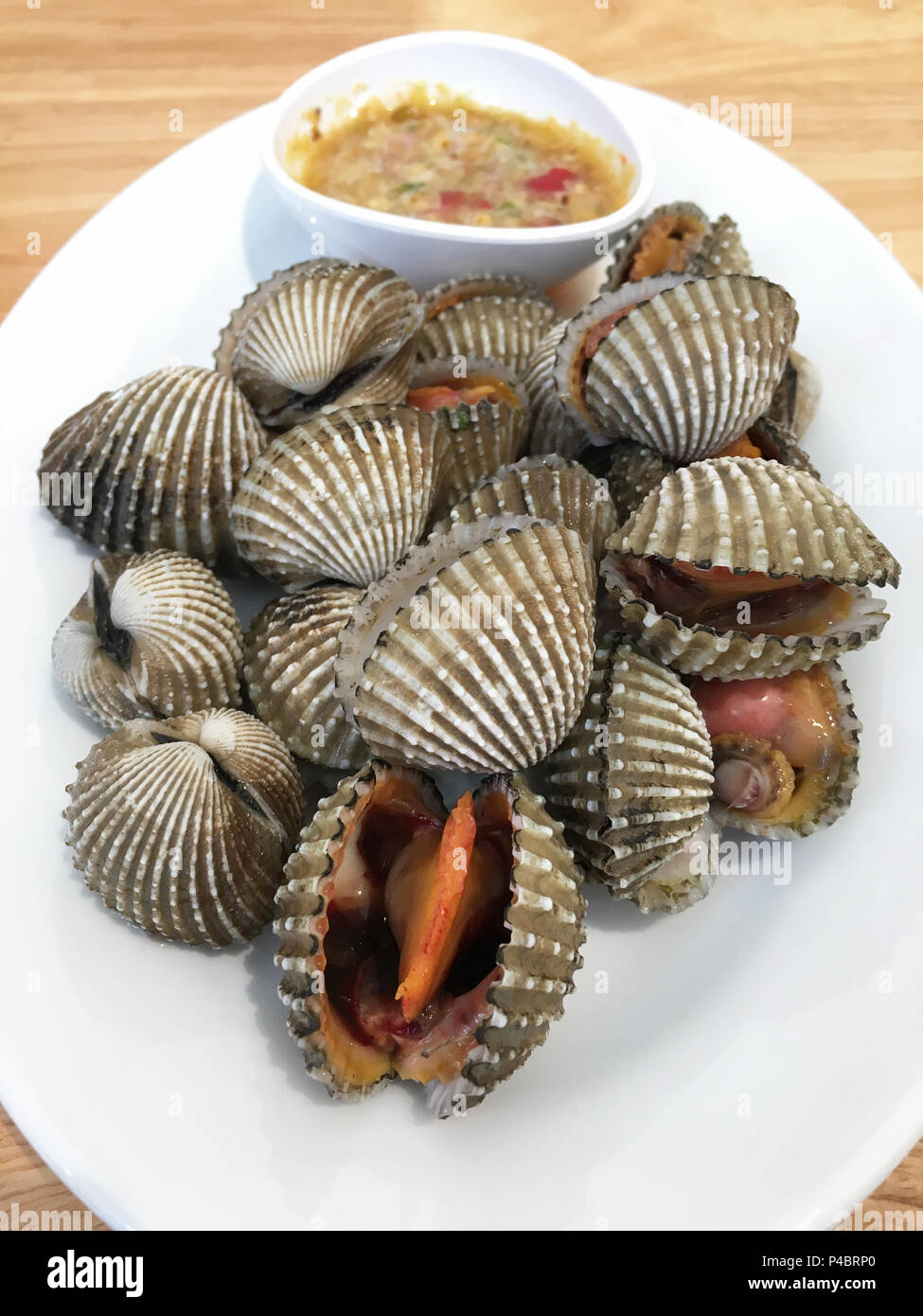 Close up fresh raw cockle shell sea food with spicy sauce on white dish ...