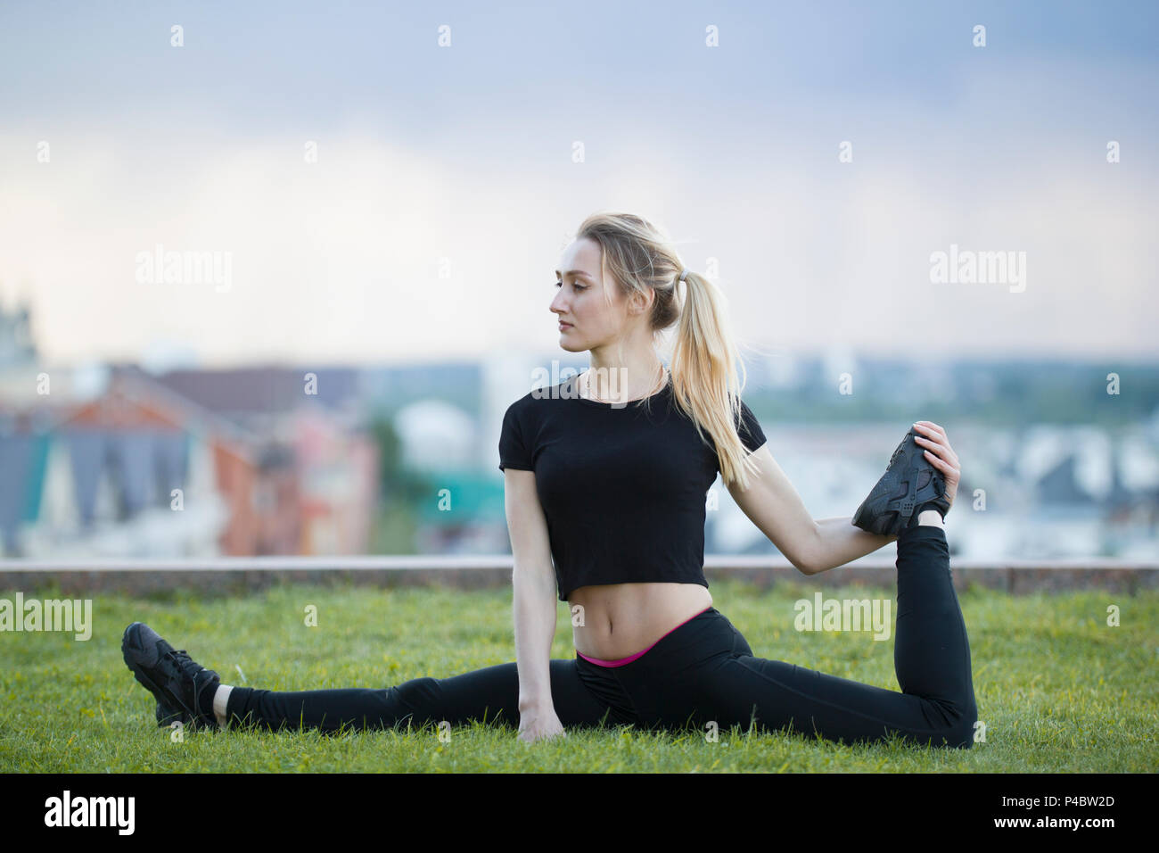 Happy young woman on the grass performs twine with the bent leg, on ...