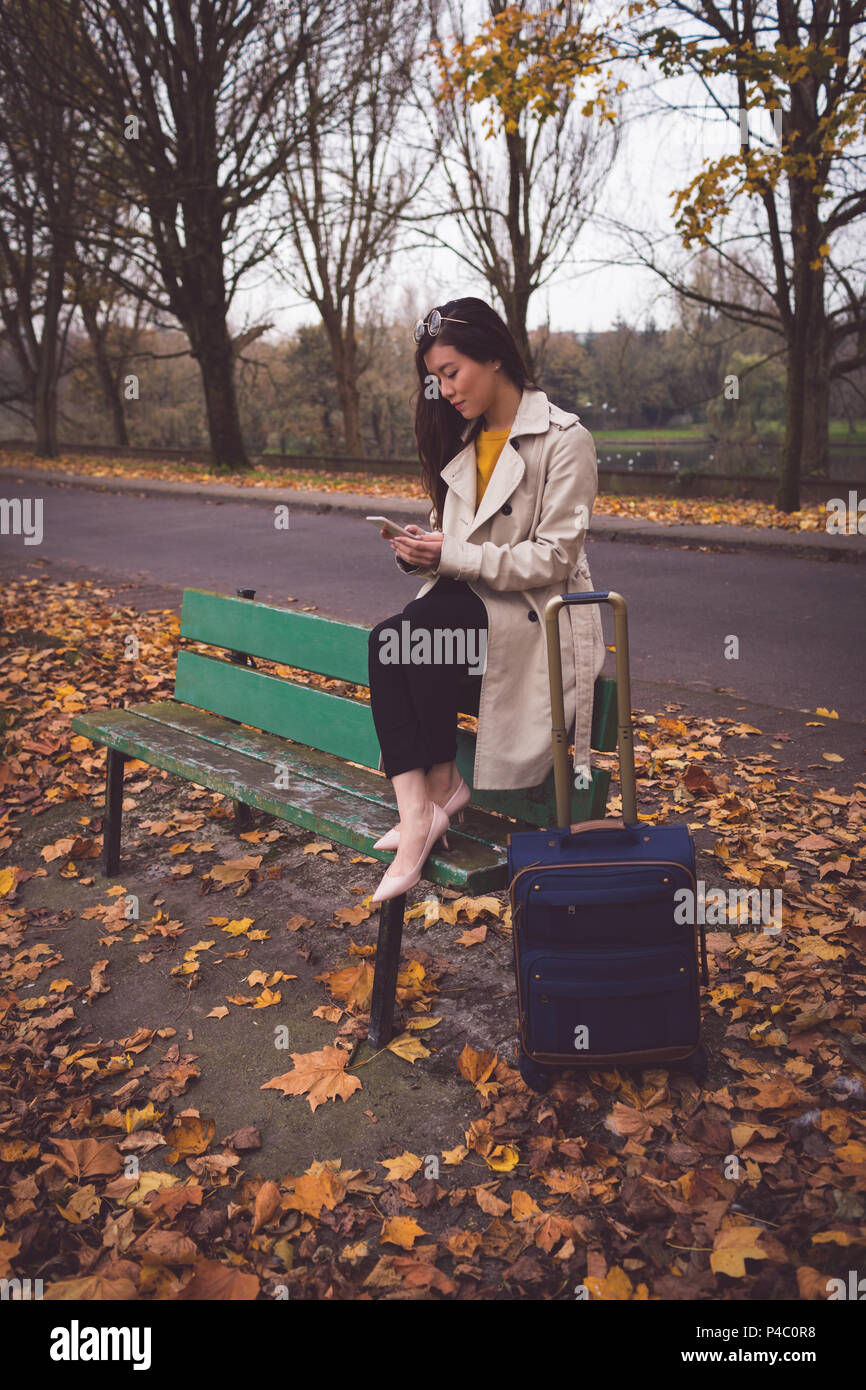 Businesswoman using mobile phone while sitting on bench Stock Photo - Alamy