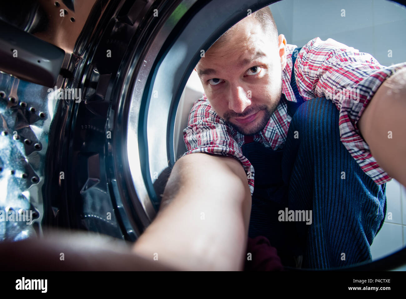 Repair man fixing the washing machine in the bathroom, view from inside ...