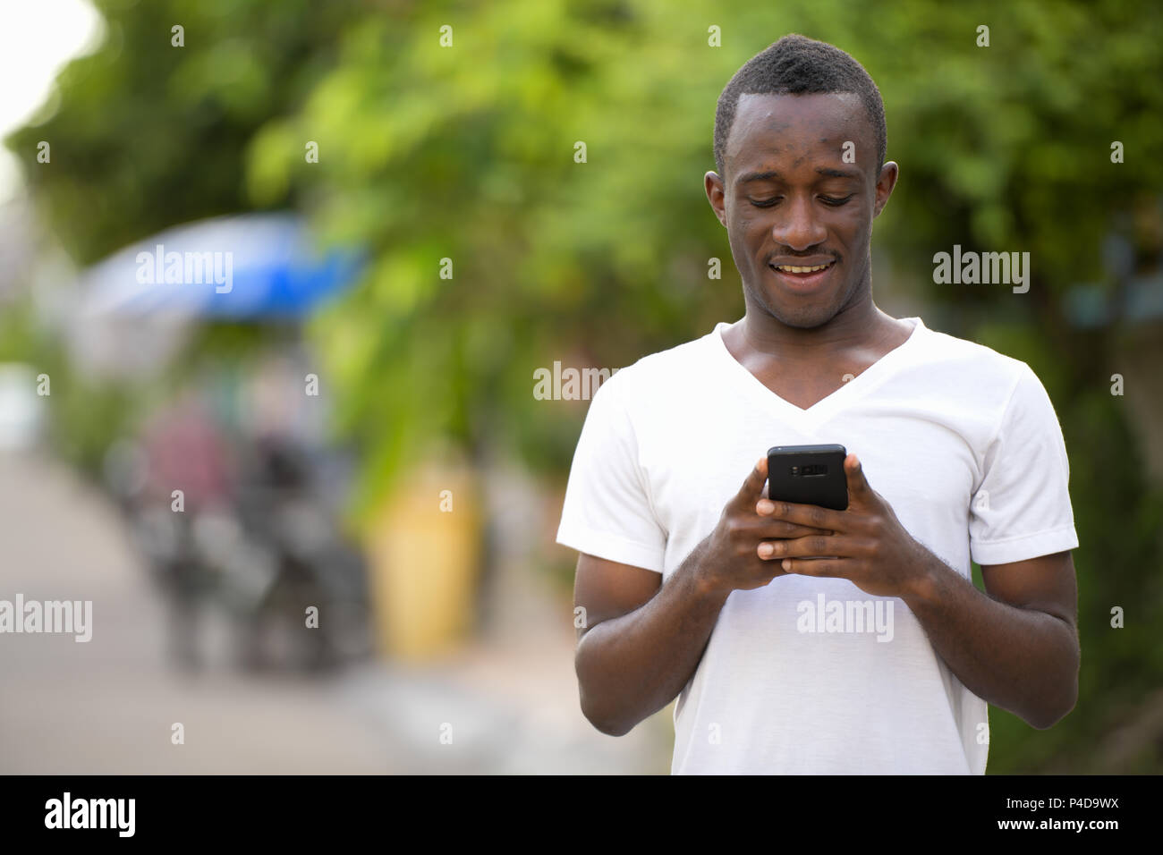 Young happy African man smiling while using phone in the streets ...