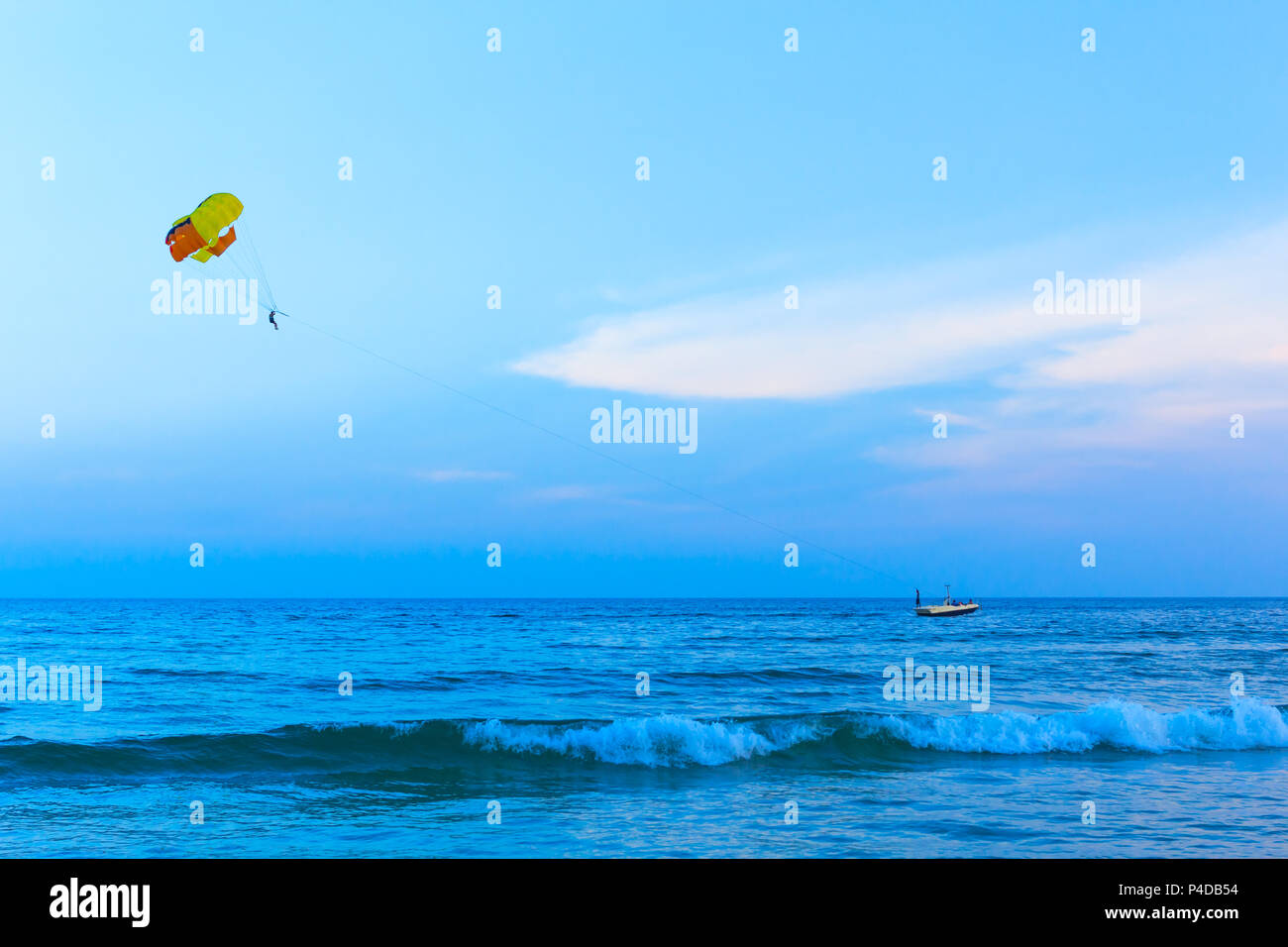 Colorful parasail wing pulled by boat in the sea water, on blue sky ...