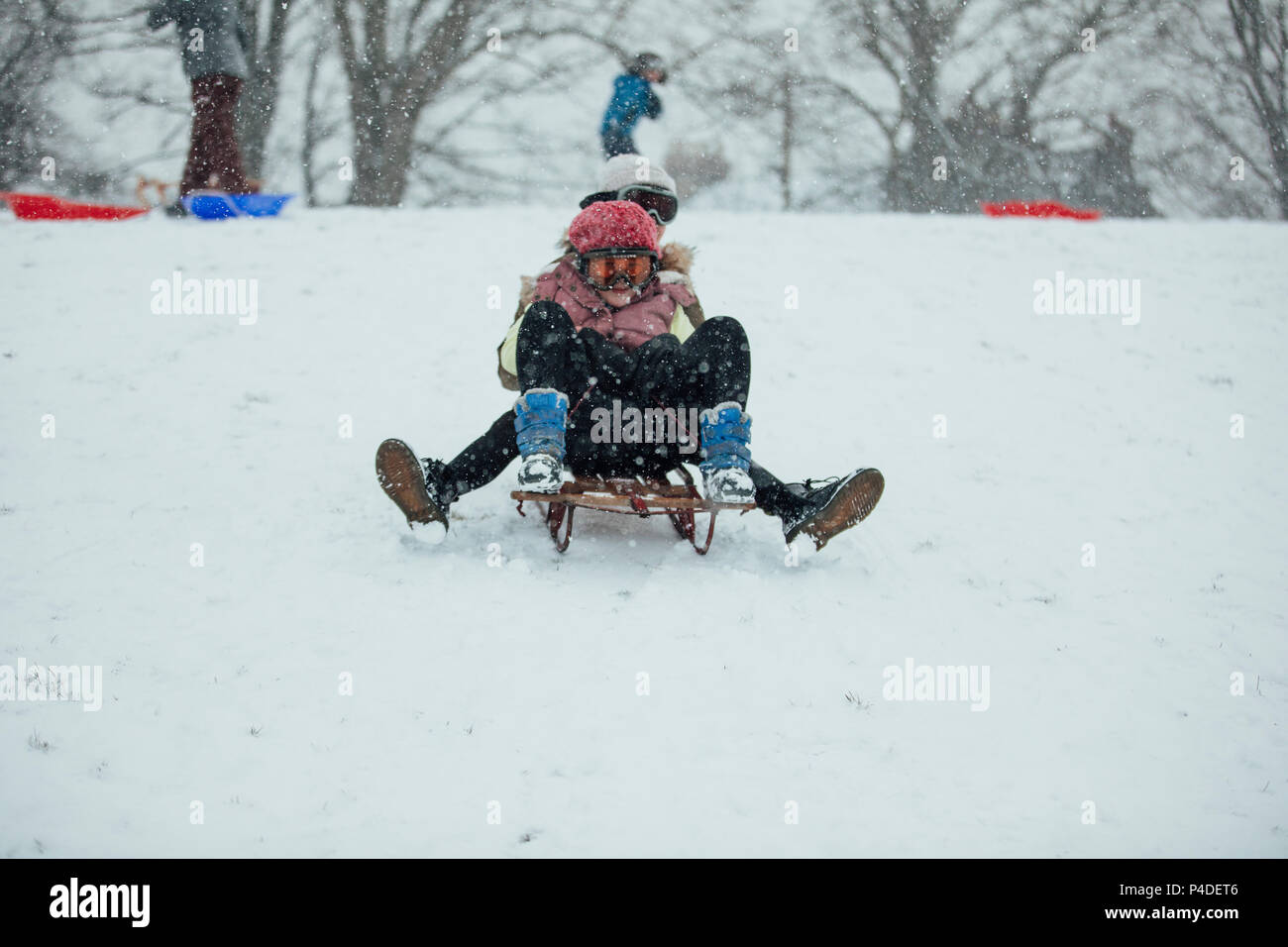 Two little girls are going down a big hill on a sled together in the ...