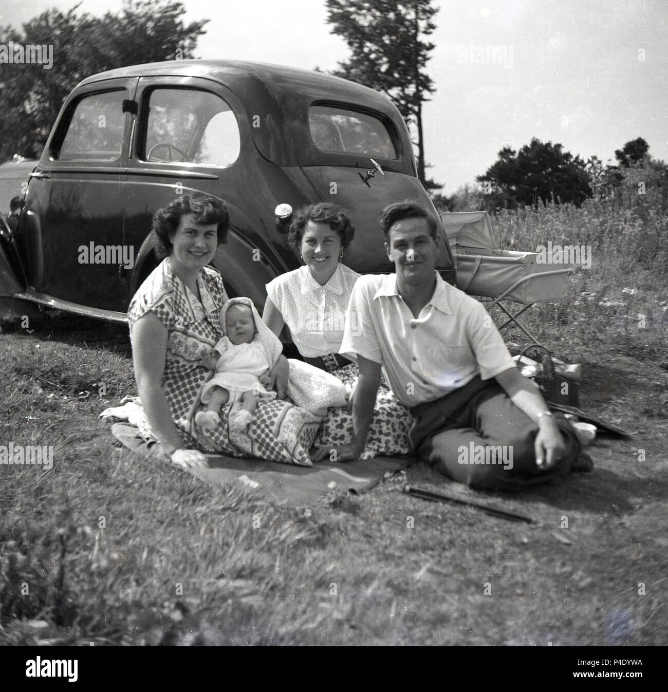 1950s, happy parents with their newborn baby and friend sit by their ...