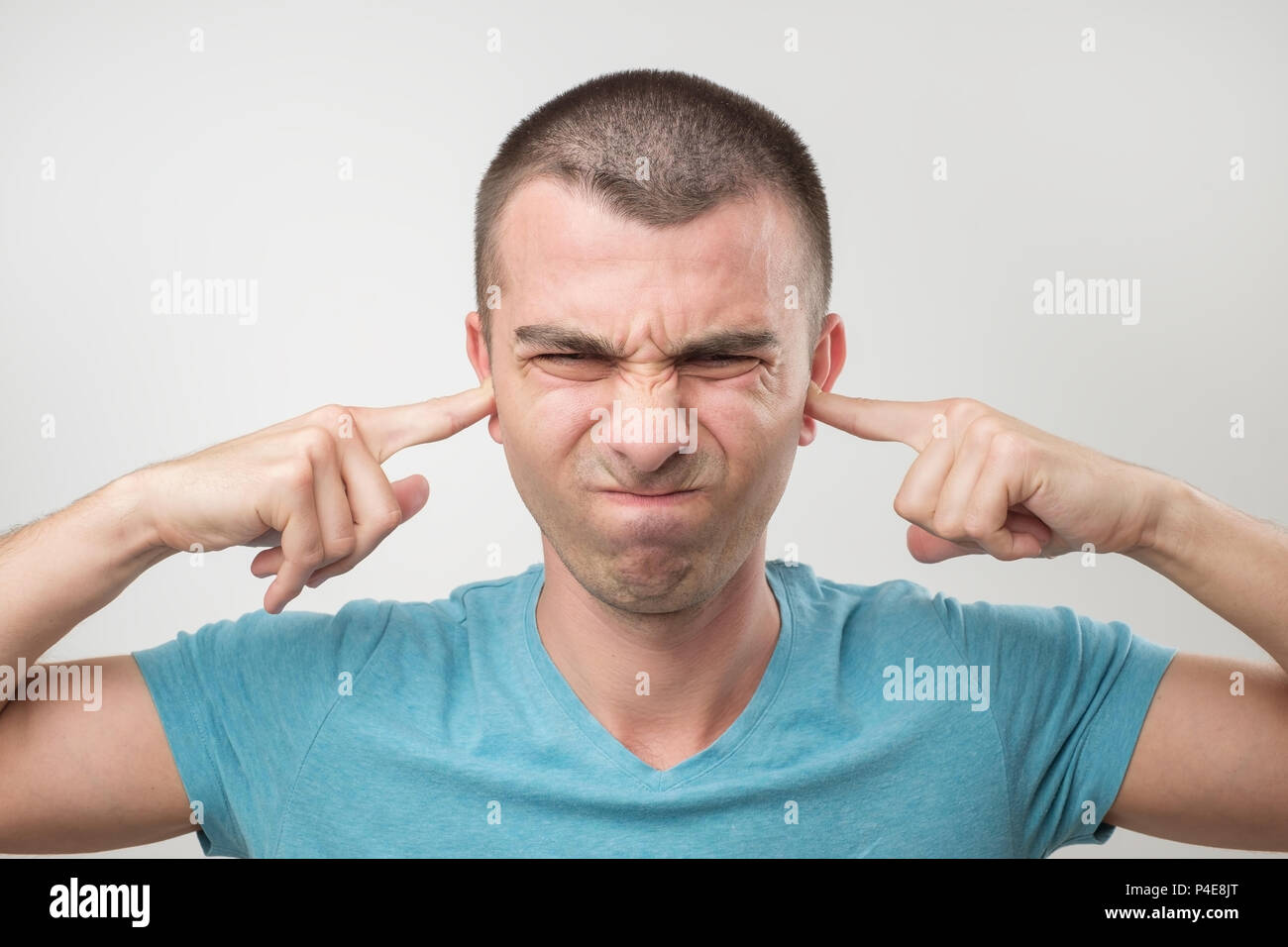 Stressed frustrated young man plugging his ears and keeping eyes closed ...