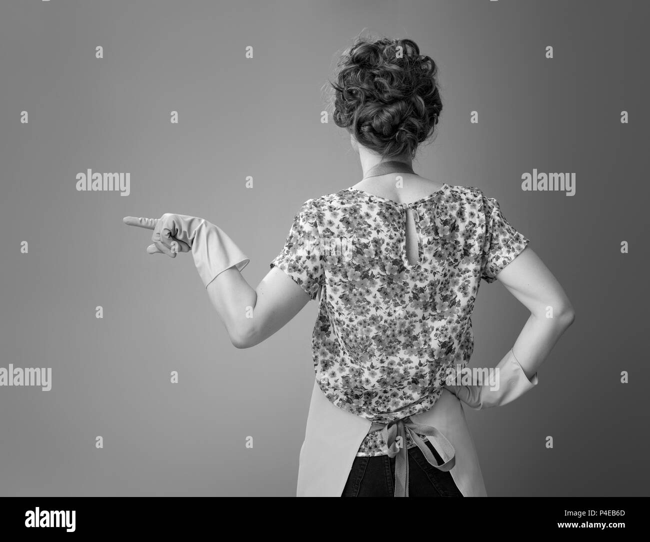 Big cleaning time. Seen from behind modern woman in a apron pointing at ...
