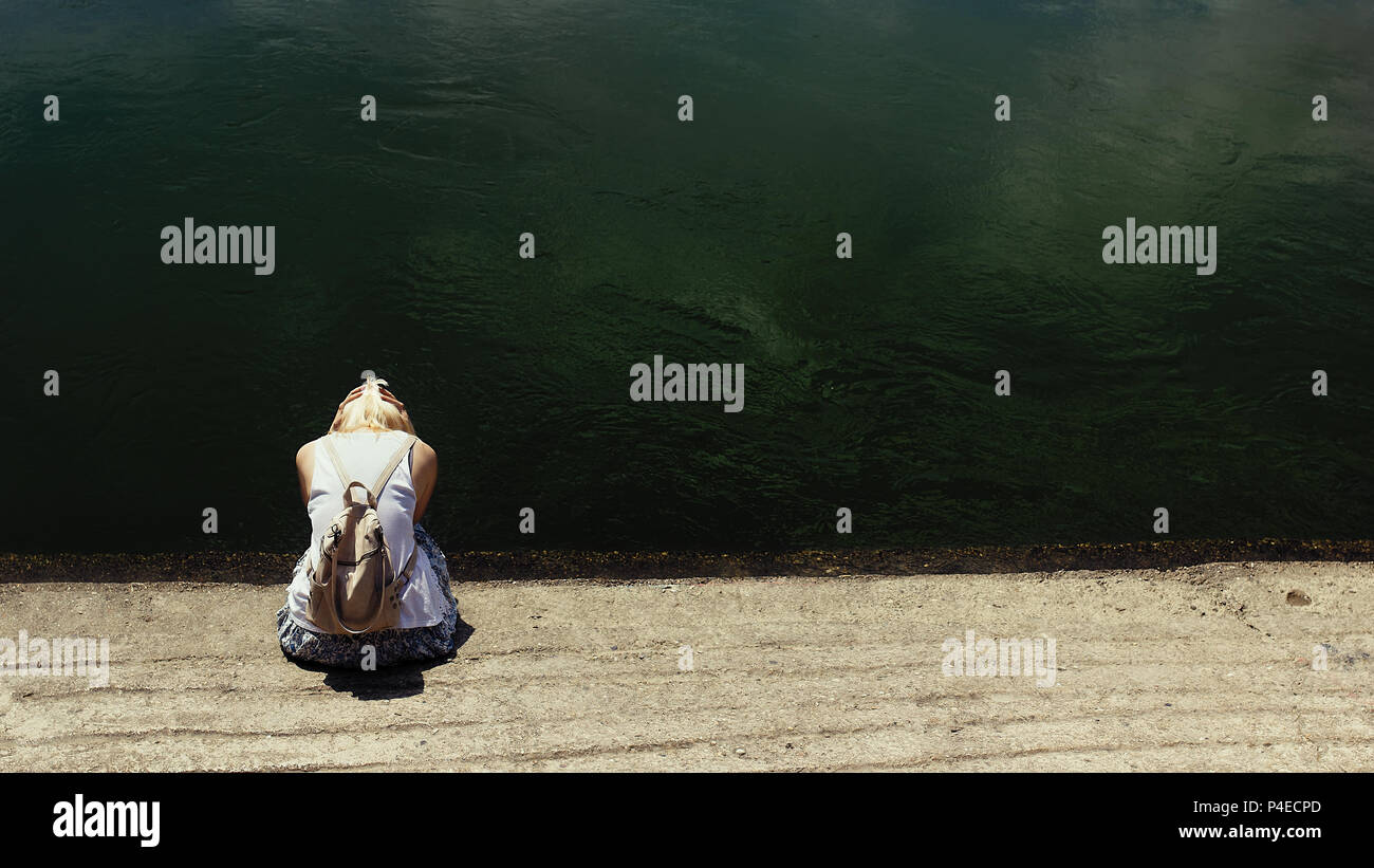 Blonde hair woman sitting by the dark river water, sad, depressed and ...